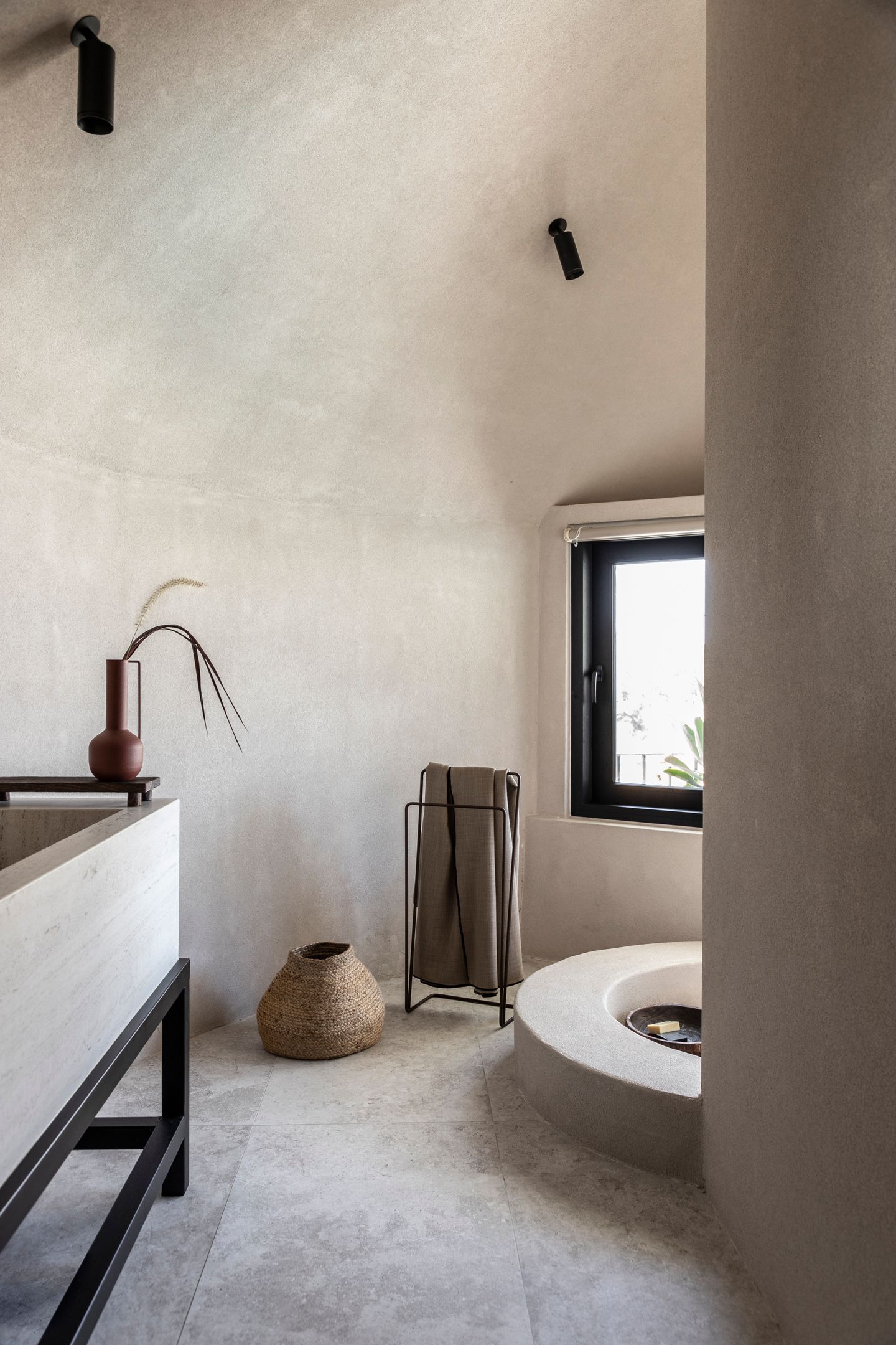 Um banheiro com piso de concreto, uma pia redonda, uma janela, porta-toalhas e um vaso com planta.