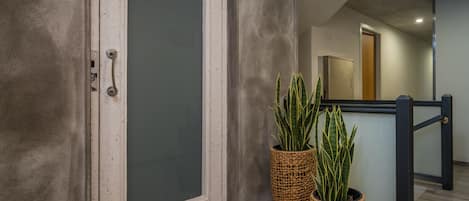 Interior moderno com porta de vidro, piso de madeira e dois cachepots de vime com plantas verdes.