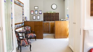 Uma área de recepção com uma mesa de madeira, certificados emoldurados, um relógio e uma estante de livros.
