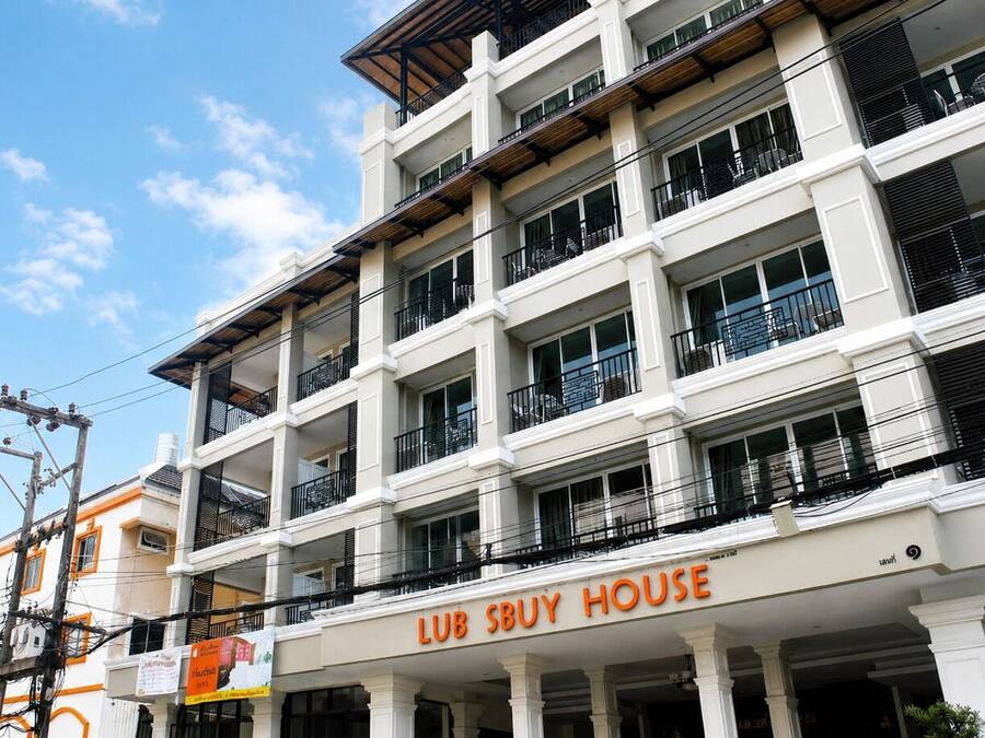Um edifício de vários andares com varandas, um letreiro com a inscrição 'LUB SBUY HOUSE' e um céu claro.