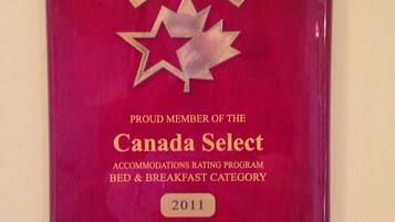 Uma placa vermelha com o texto "Membro orgulhoso do Programa de Classificação de Acomodações Canada Select, Categoria Bed & Breakfast 2011" e cinco estrelas abaixo.