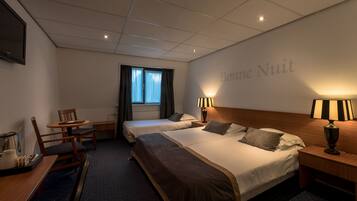 Quarto de hotel com duas camas, uma escrivaninha, uma cadeira e janela com cortinas.
