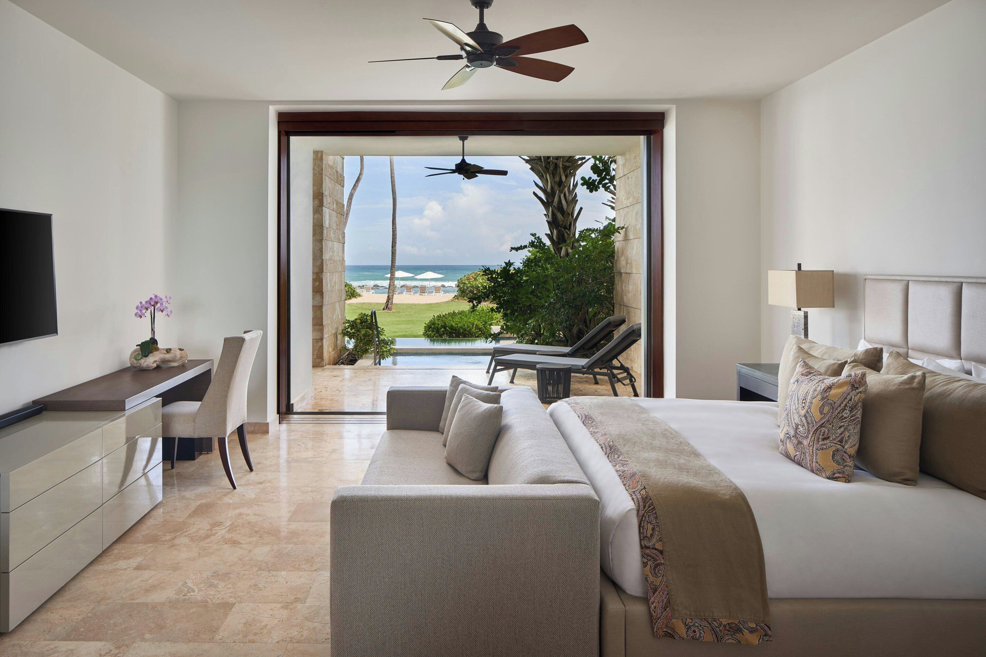 Quarto de hotel moderno com cama, escrivaninha, cadeira e vista para a praia.