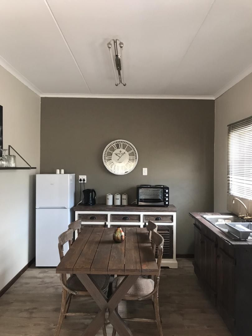 Uma cozinha compacta com mesa de madeira, cadeiras, relógio, torradeira e geladeira.