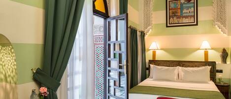 Quarto de hotel com cama, duas luminárias de cabeceira, bandeja com garrafa e copos, e janela com cortinas.