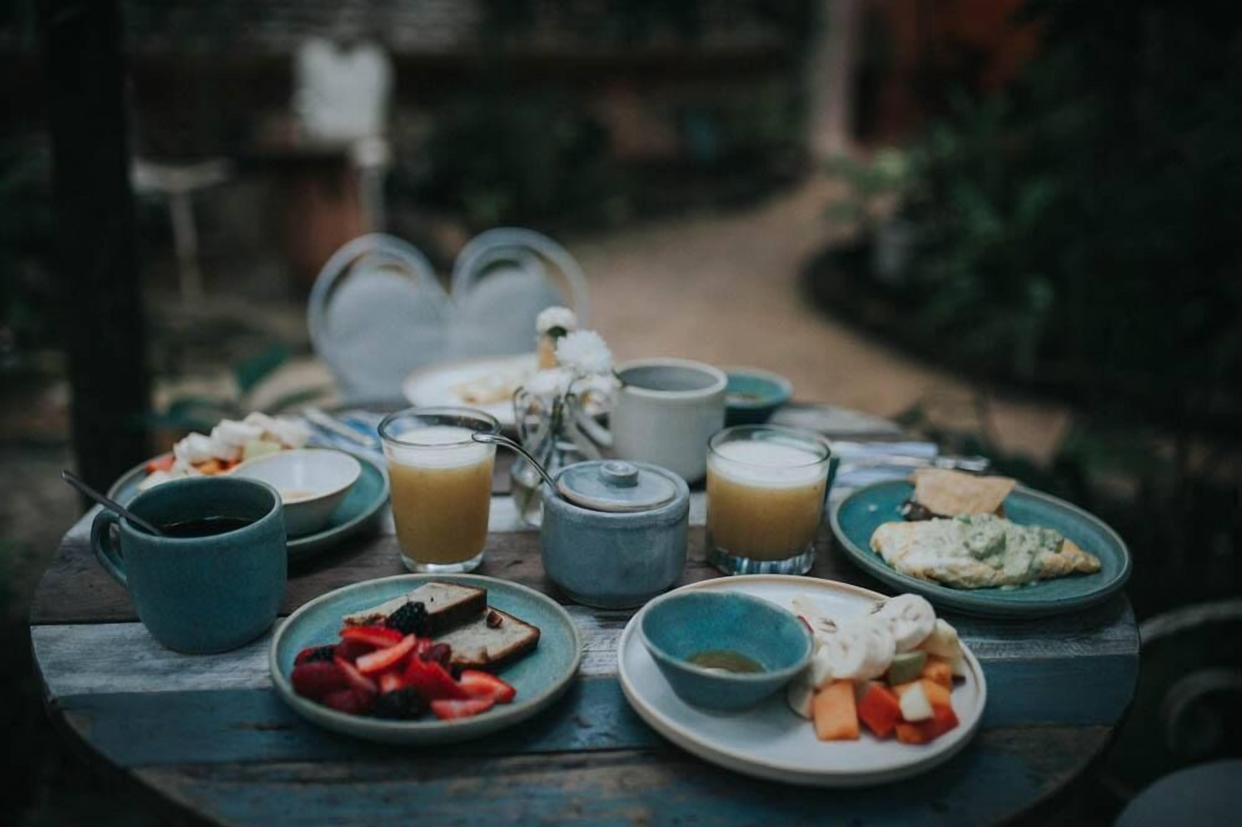 Uma mesa rústica ao ar livre com diversos pratos, bebidas e uma chaleira.