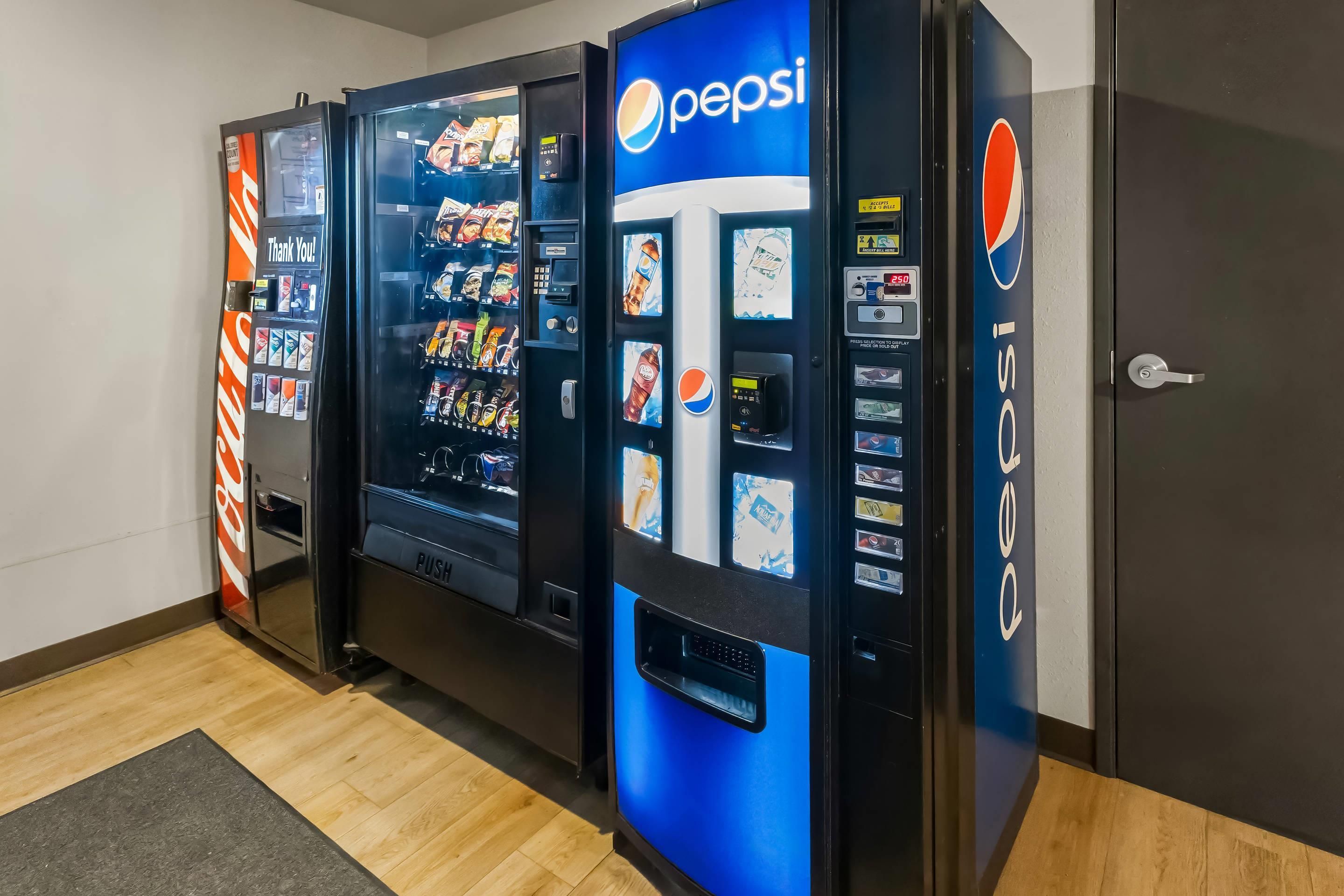 Três máquinas de venda automática com a marca Pepsi, uma com fundo azul e as outras com fundo laranja e preto.