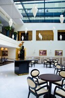 Um hall amplo com teto alto, luminárias modernas, áreas de estar e obras de arte nas paredes.