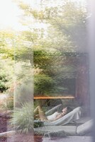 Uma pessoa relaxando em uma rede em um jardim com árvores e plantas ao redor.