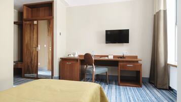 Quarto de hotel com cama, escrivaninha, cadeira, televisão e guarda-roupa.