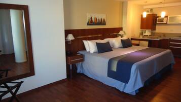 Quarto de hotel com uma cama grande, mesa de cabeceira, escrivaninha, cadeira, espelho, quadro, micro-ondas e pia.