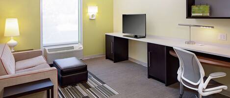 Quarto de hotel moderno com sofá, escrivaninha com computador, televisão e luminária.