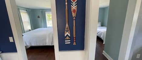 Quarto com uma cama, um remo fixado na parede e uma janela com cortinas.