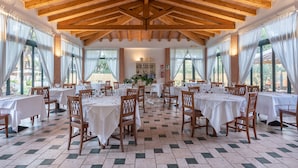 Uma sala de jantar espaçosa com mesas e cadeiras de madeira, janelas amplas e um alto teto de madeira.