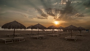 Uma praia com guarda-sóis de palha e espreguiçadeiras sob um céu ao pôr do sol.