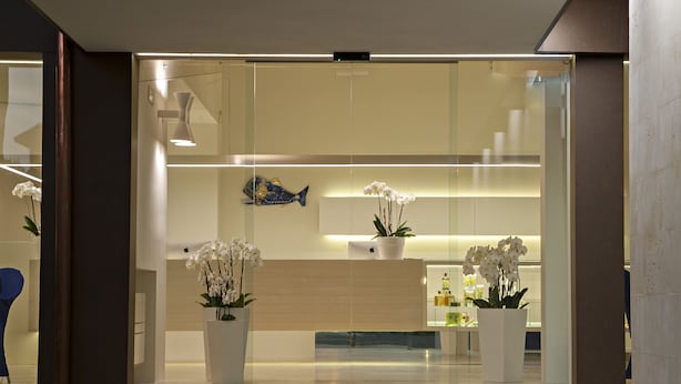 Uma área de recepção moderna com portas de vidro, orquídeas brancas em vasos e uma decoração de peixe azul.