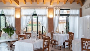 Um restaurante com várias mesas e cadeiras, toalhas de mesa brancas e paredes de tijolos.
