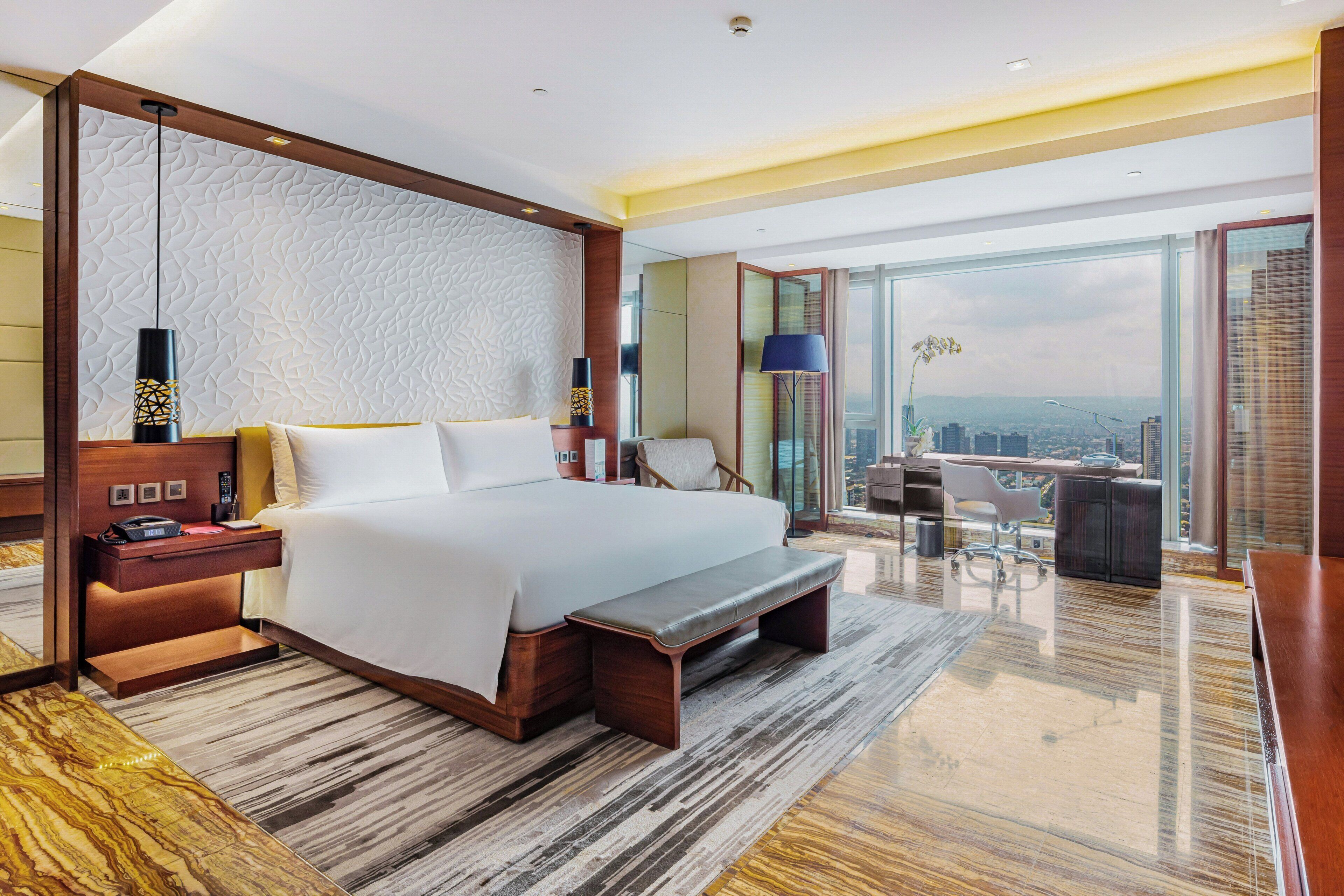 Quarto de hotel moderno com uma cama grande, uma escrivaninha e vista para a cidade.