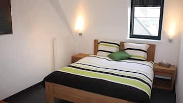 Quarto com cama, duas mesas de cabeceira, janela e luminárias fixadas na parede.