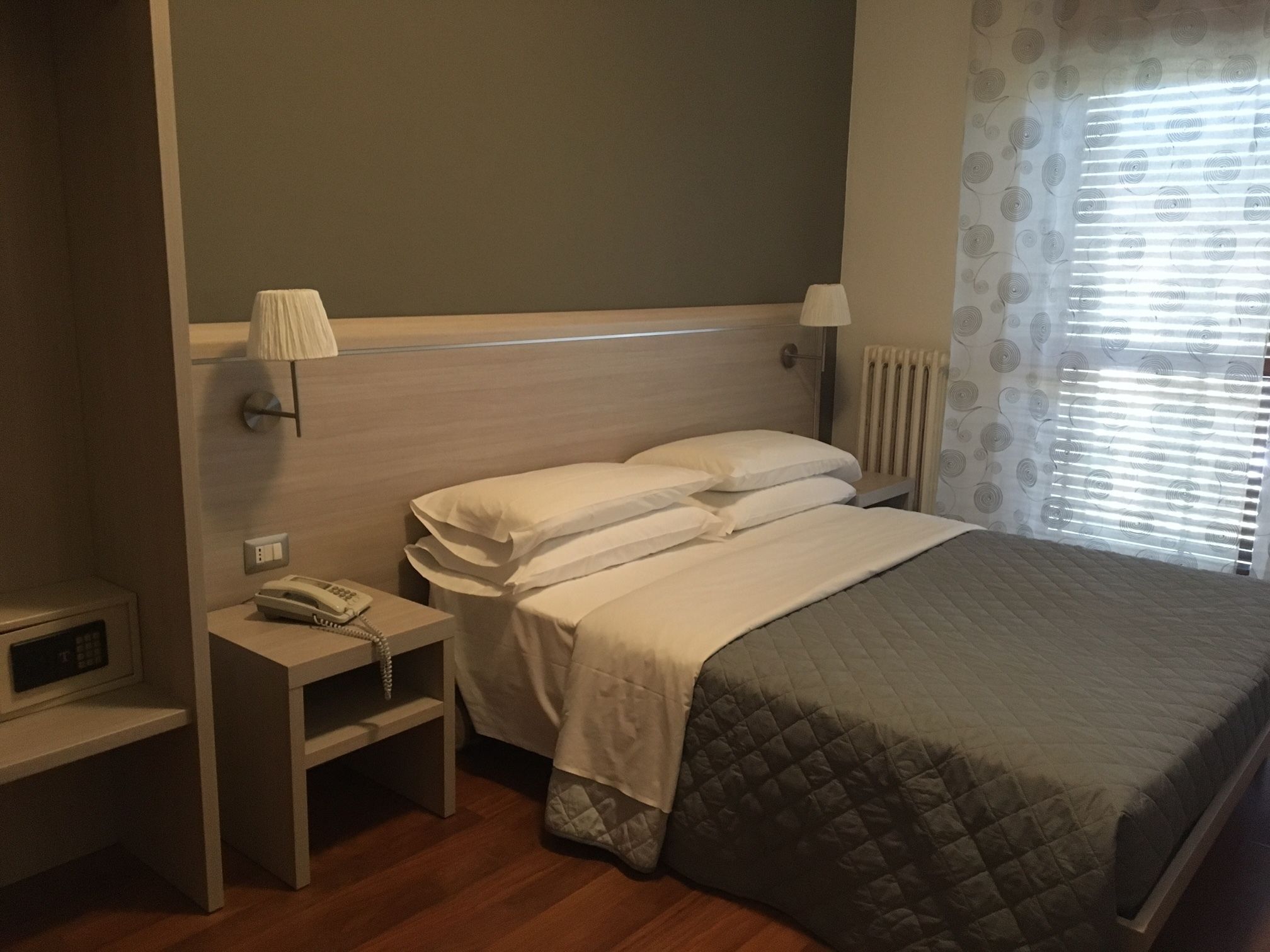 Quarto de hotel com cama, abajures, telefone e radiador.