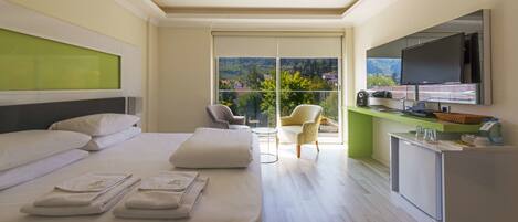 Quarto de hotel moderno com uma cama grande, área de estar com uma poltrona, televisão e varanda com vista para as montanhas.