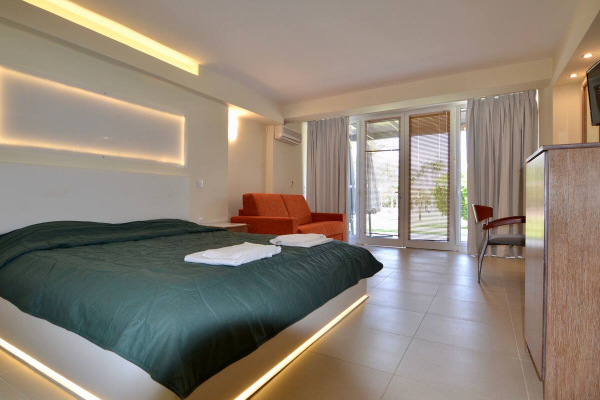Quarto de hotel moderno com uma cama grande, área de estar com uma poltrona e vista através das portas de vidro.