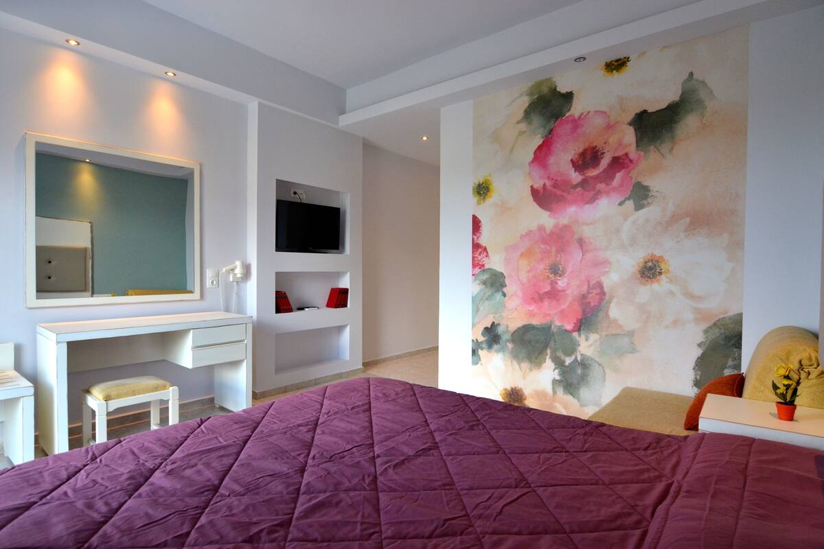 Um quarto com uma cama, uma escrivaninha, uma cadeira, uma televisão e um grande mural floral na parede.