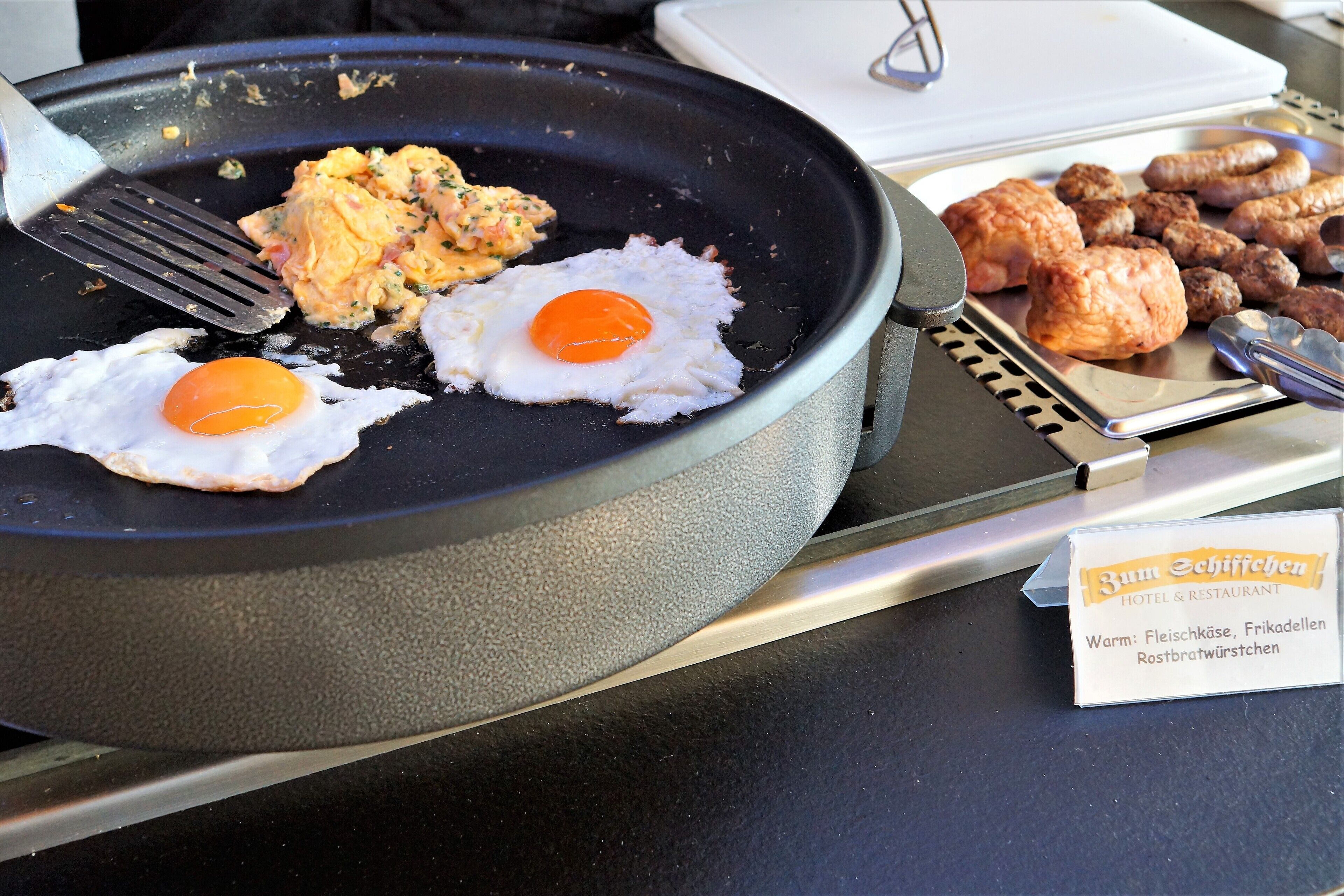 Uma mesa de café da manhã com ovos, salsichas e ovos mexidos em uma frigideira.