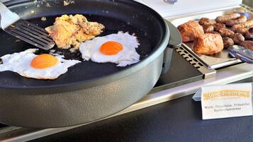 Uma mesa de café da manhã com ovos, salsichas e ovos mexidos em uma frigideira.