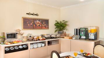 Buffet de café da manhã com diversas opções de alimentos, uma máquina de café e um quadro na parede.