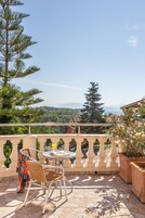 Terraço com mesa e cadeiras, com vista para uma paisagem montanhosa.