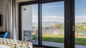Quarto de hotel moderno com uma grande porta de correr de vidro que dá para uma varanda com vista panorâmica.