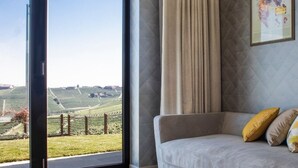 Quarto com uma grande porta de vidro deslizante que dá para vista de um vinhedo, sofá cinza com almofadas e um mapa emoldurado na parede.