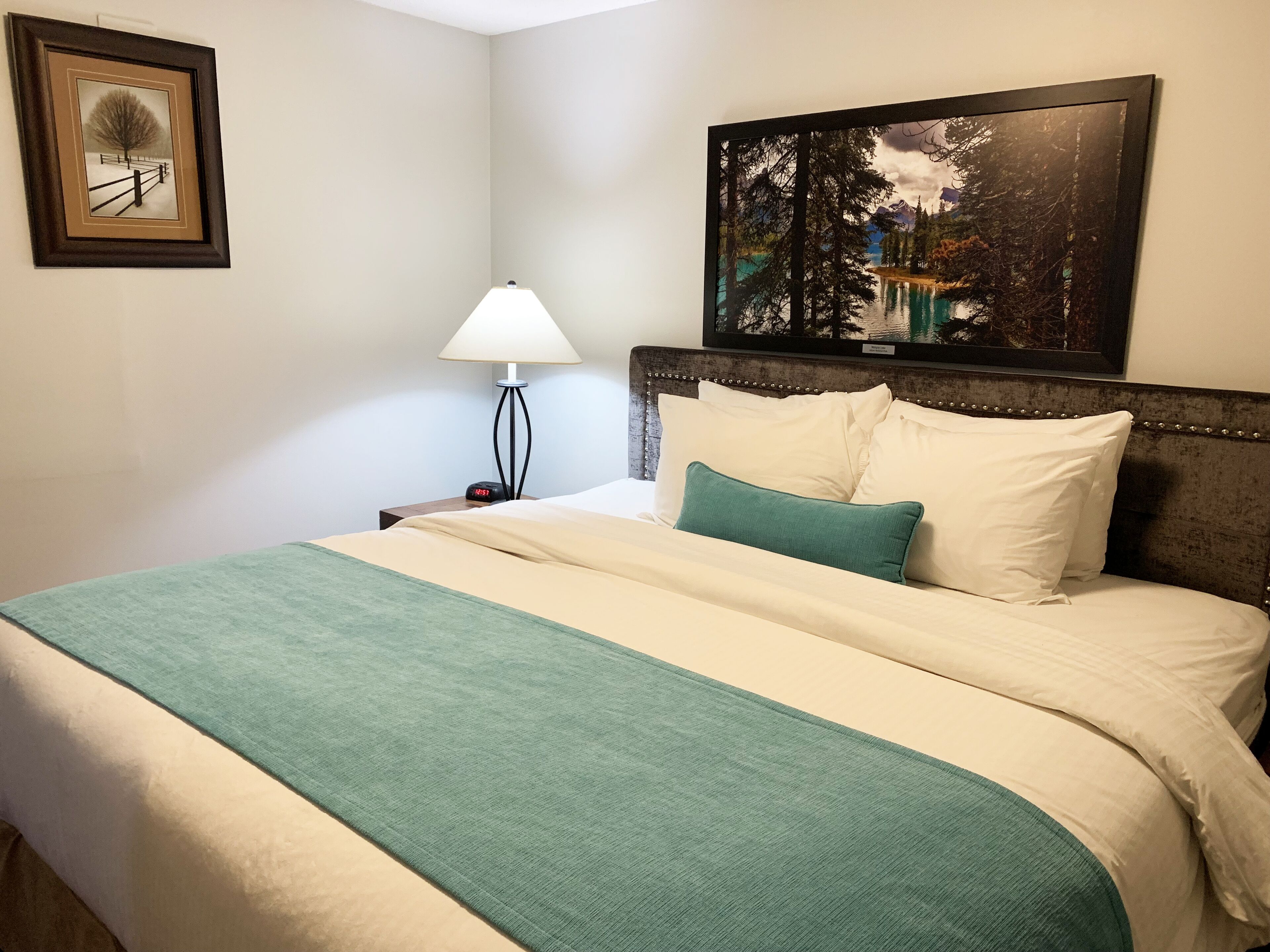 Cama bem arrumada com manta verde, almofadas brancas e cabeceira com uma pintura em cima.