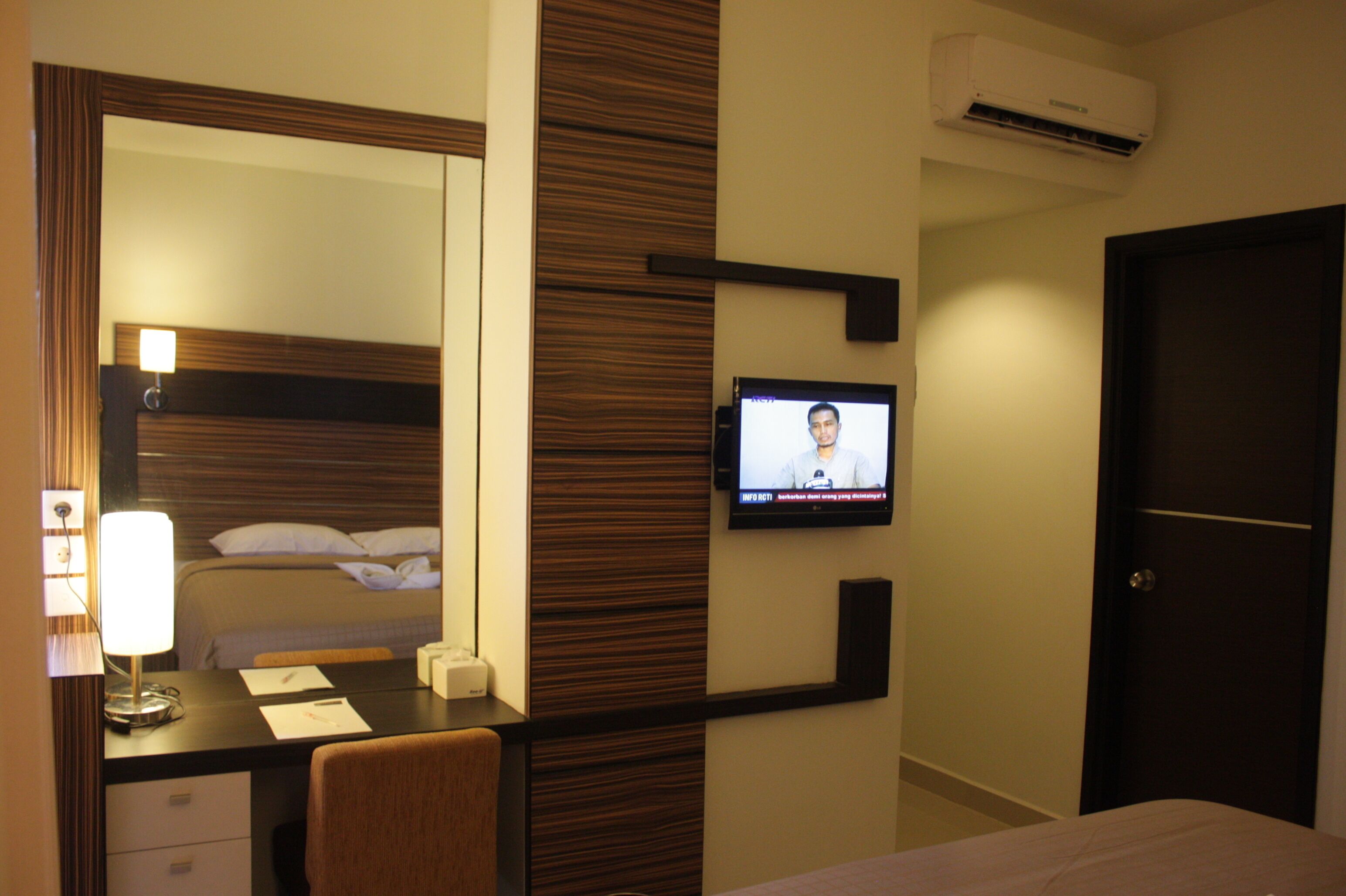 Quarto de hotel com cama, escrivaninha com luminária, televisão na parede e ar condicionado.