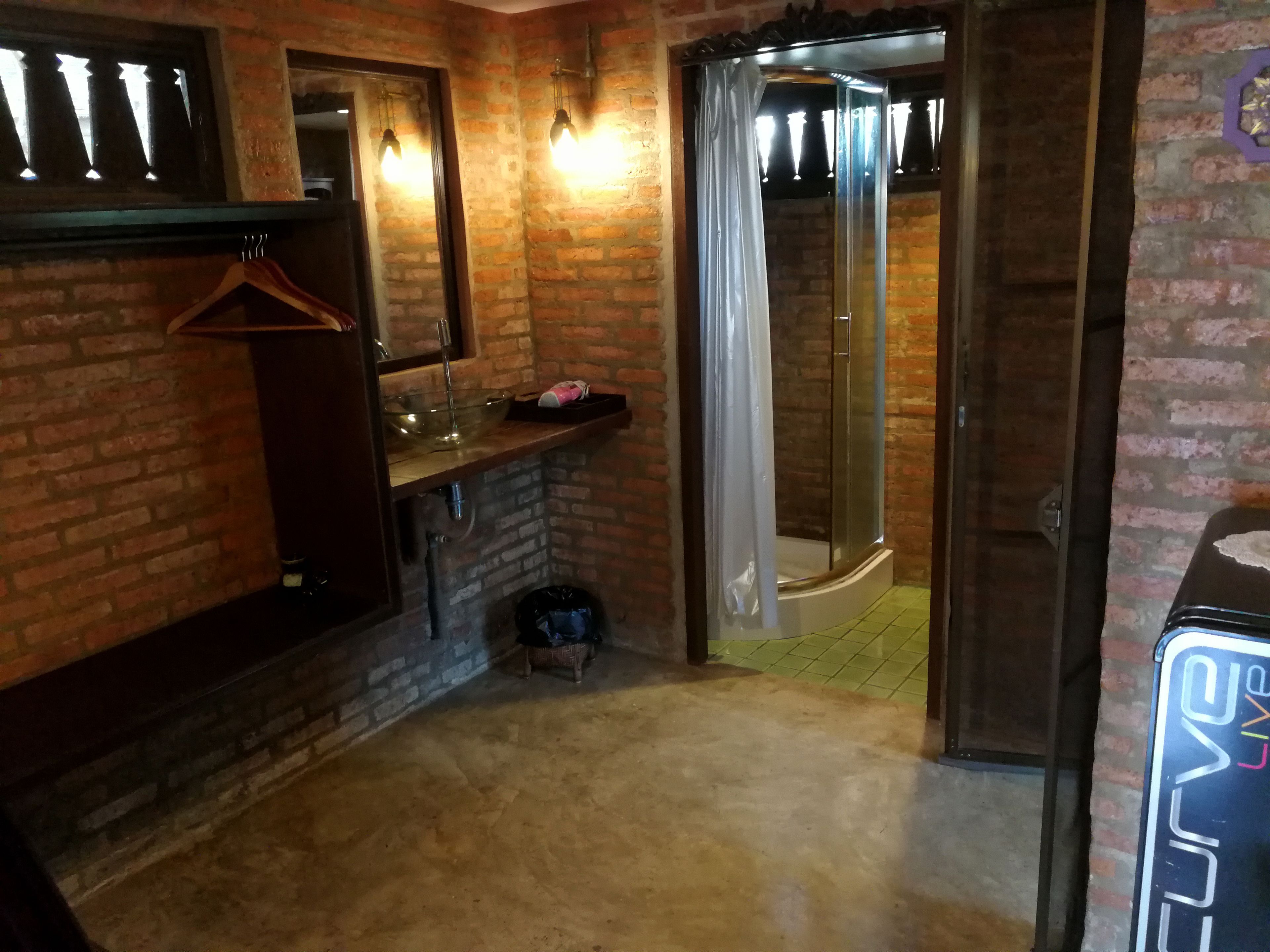 Casa de banho com parede de tijolos, cabine de chuveiro em vidro, lavatório e suporte para toalhas.