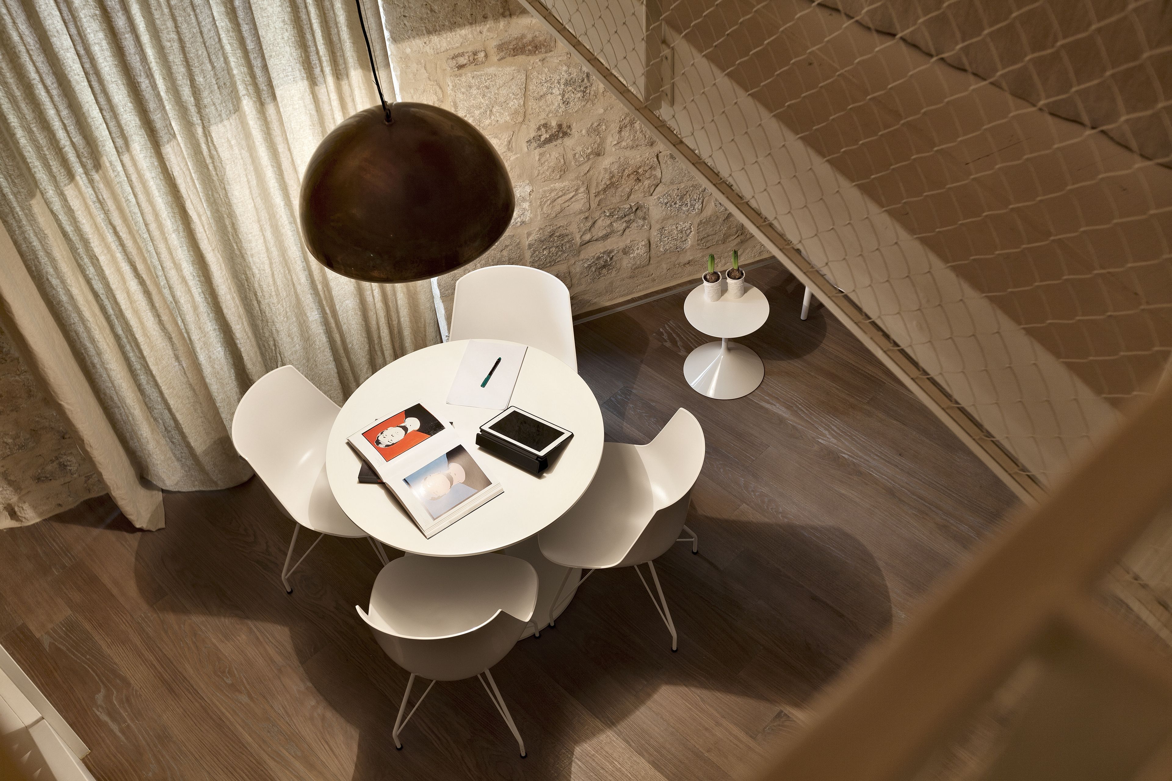 Uma área de refeições moderna com uma mesa redonda, cadeiras brancas e uma luminária pendente.