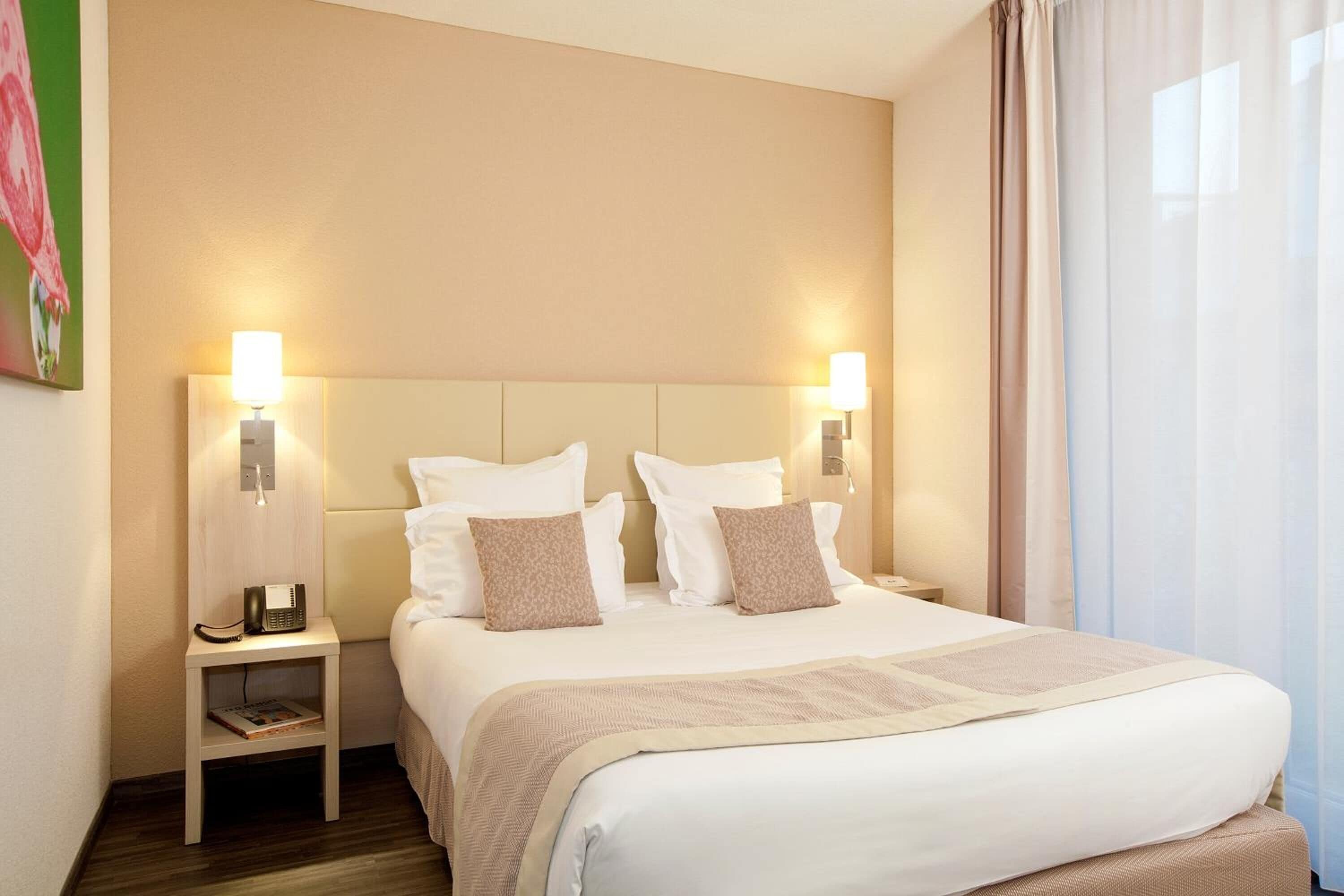 Quarto de hotel com uma cama grande, duas mesas de cabeceira com luminárias, uma mesinha de apoio com telefone e um quadro na parede.