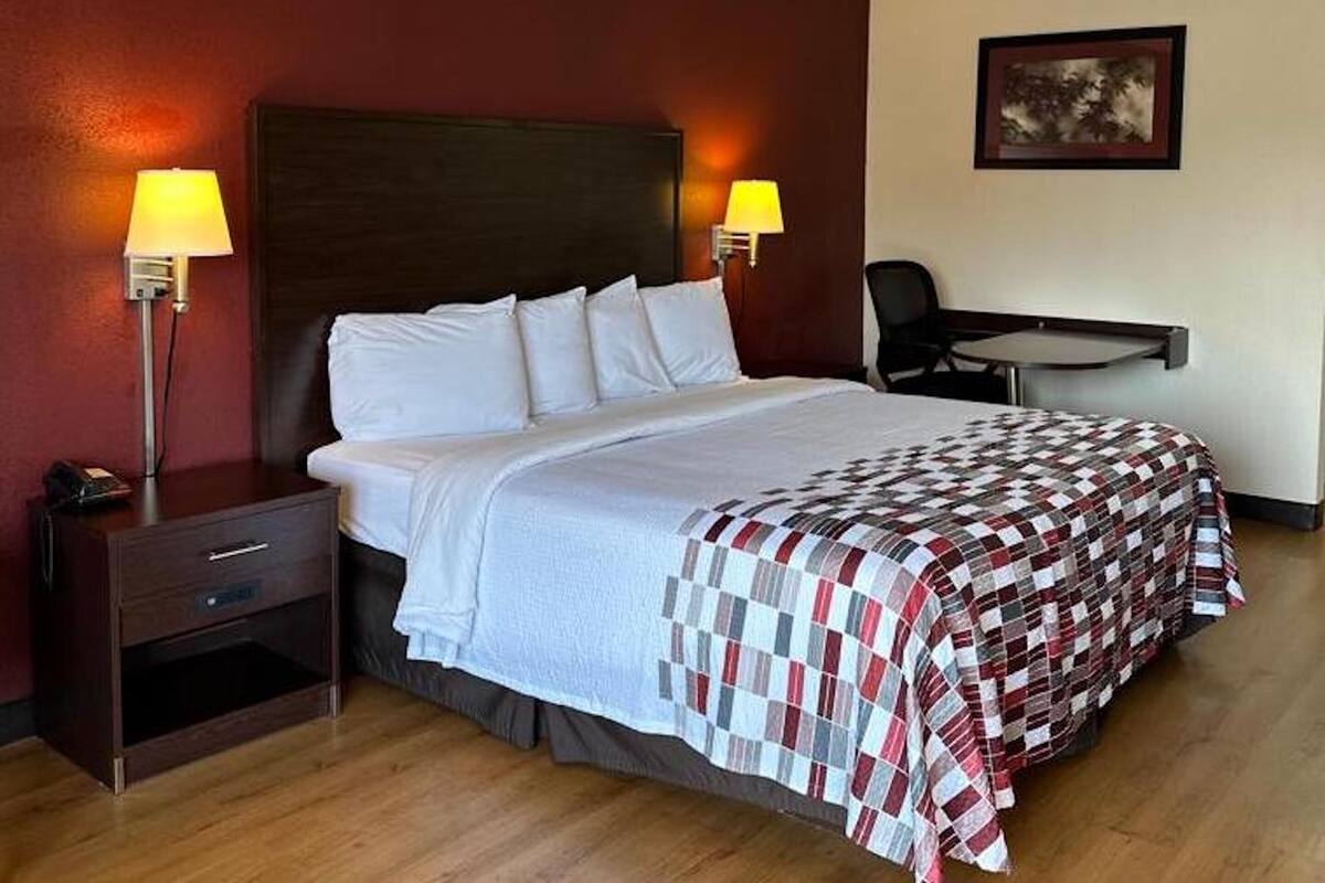 Quarto de hotel com uma cama grande, duas luminárias de cabeceira, uma escrivaninha pequena e uma cadeira.