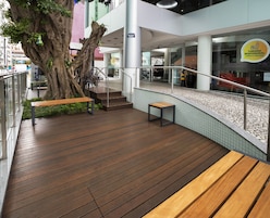 Um espaço interno moderno com piso de madeira, uma grande árvore e bancos.