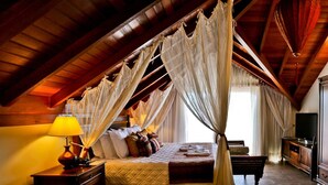 Quarto com cama de dossel, vigas de madeira no teto, mesa de cabeceira com luminária, televisão e armário de madeira.