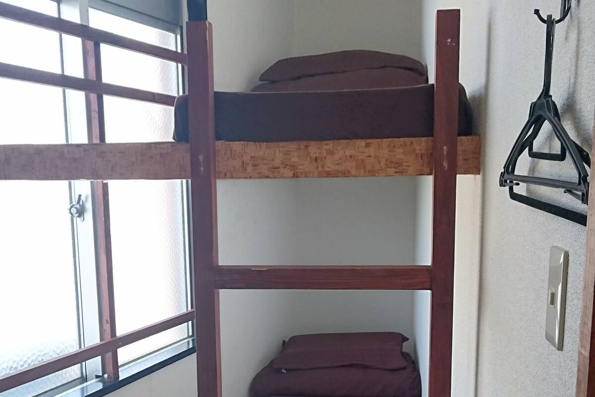Quarto com beliche, janela e cabide fixado na parede.