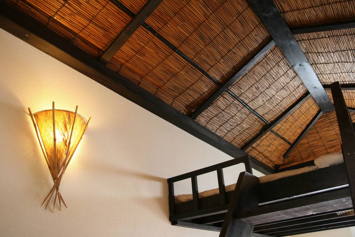 Um quarto com teto alto, telhado de palha e cama com estrutura de madeira.