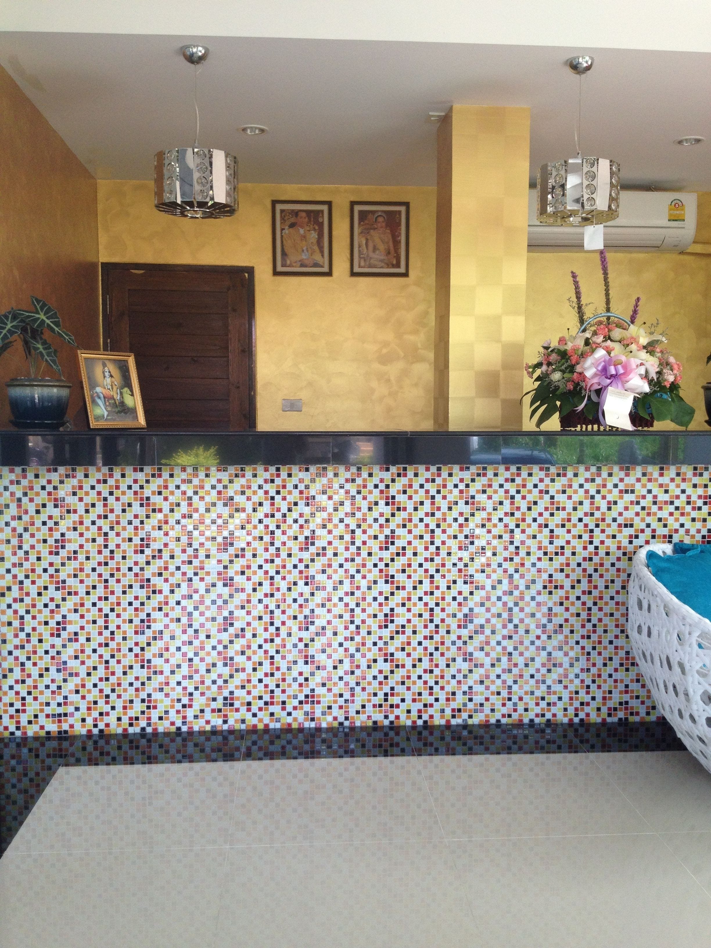 Uma área de recepção com parede de azulejos em mosaico, quadros nas paredes, uma planta em vaso e um arranjo floral.