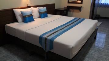 Uma cama bem arrumada com colcha listrada em branco e azul, dois travesseiros e uma mesinha de cabeceira com abajur.