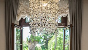 Um quarto com porta de vidro que dá para um jardim, uma mesa redonda com um buquê, e um lustre.