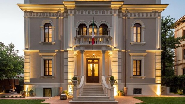 Um edifício imponente e clássico, com fachada simétrica, entrada central com degraus e um gramado bem cuidado com iluminação cênica.