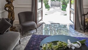 Um quarto amplo com um lustre grande, um sofá, uma mesa com um arranjo de flores e vista para um jardim através de portas abertas.