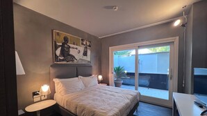 Quarto moderno com cama, mesas de cabeceira, um quadro e porta de vidro deslizante para uma varanda.