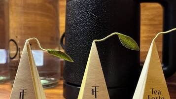 Três caixas de chá com as etiquetas 'Jasmine Green', 'White Ginger Pear' e 'Tea Forte' sobre uma superfície de madeira, com uma chaleira preta 'MEISON' ao fundo.